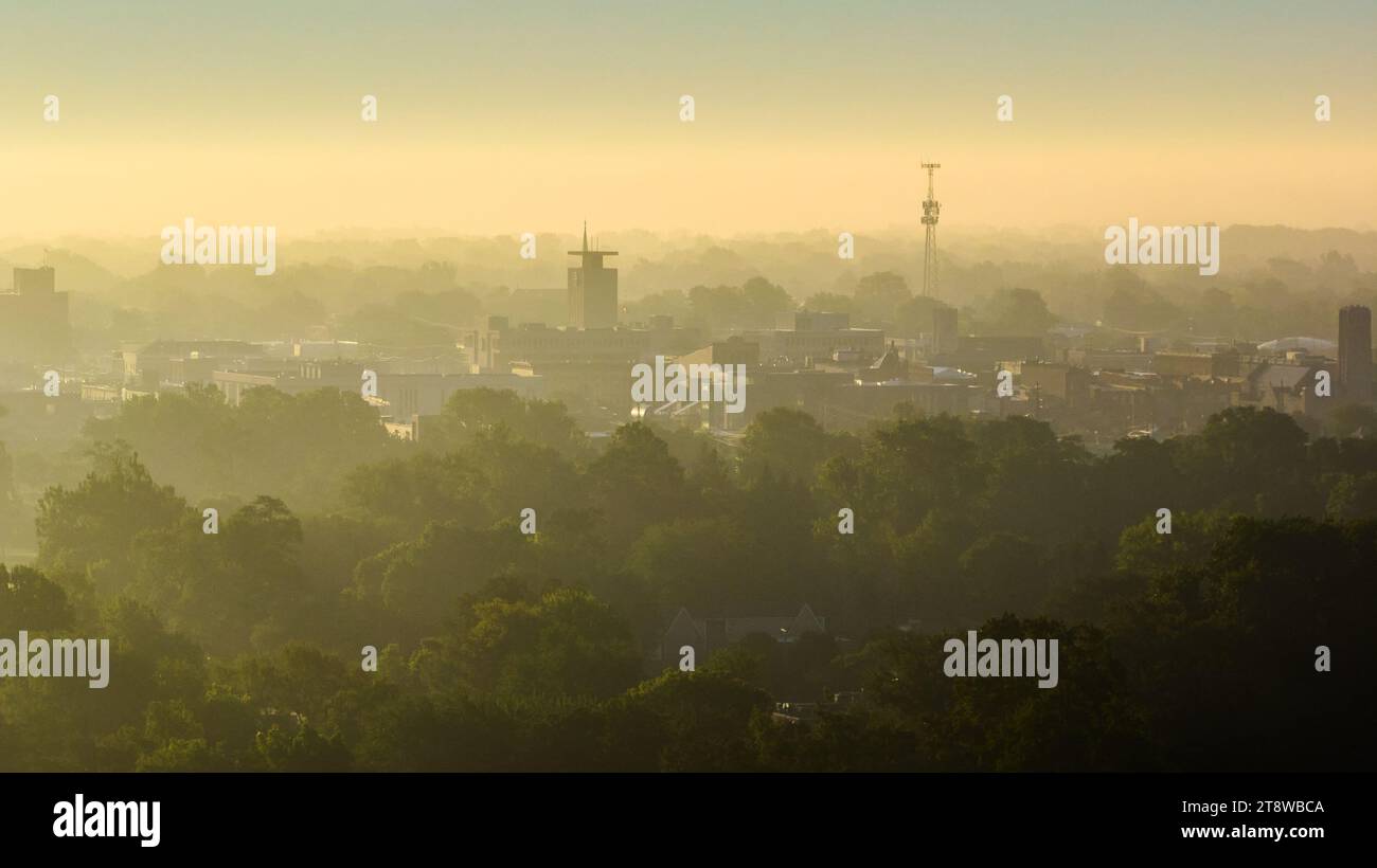 Hazy yellow sunrise with smog over city and green summer trees in ...