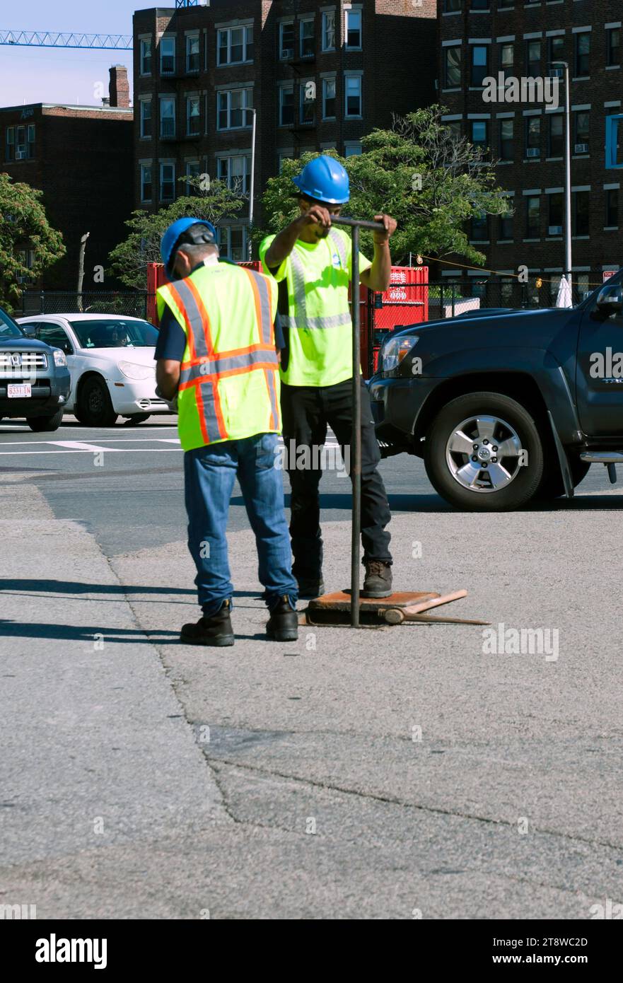 Two workmen opening a valve in the middle of the road, whilst a ...