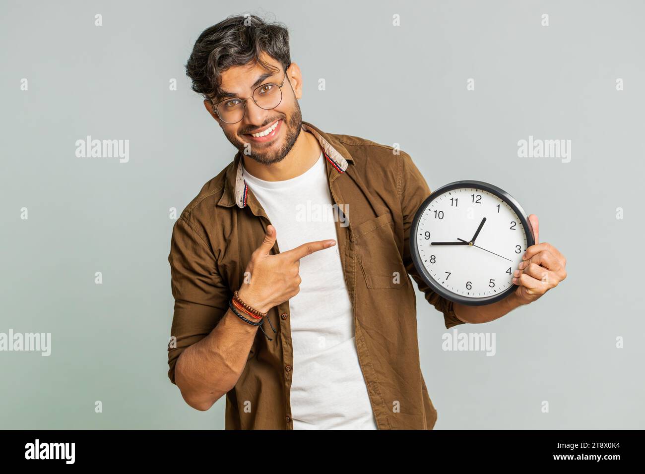 It is your time, hurry up. Indian young man showing time on wall office clock, ok, thumb up ...