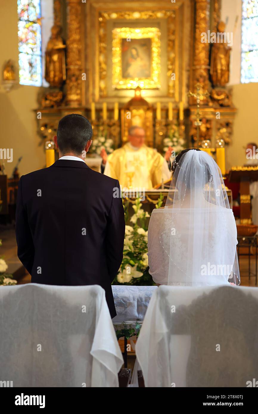 A young couple stands in front of the altar during a wedding ceremony ...