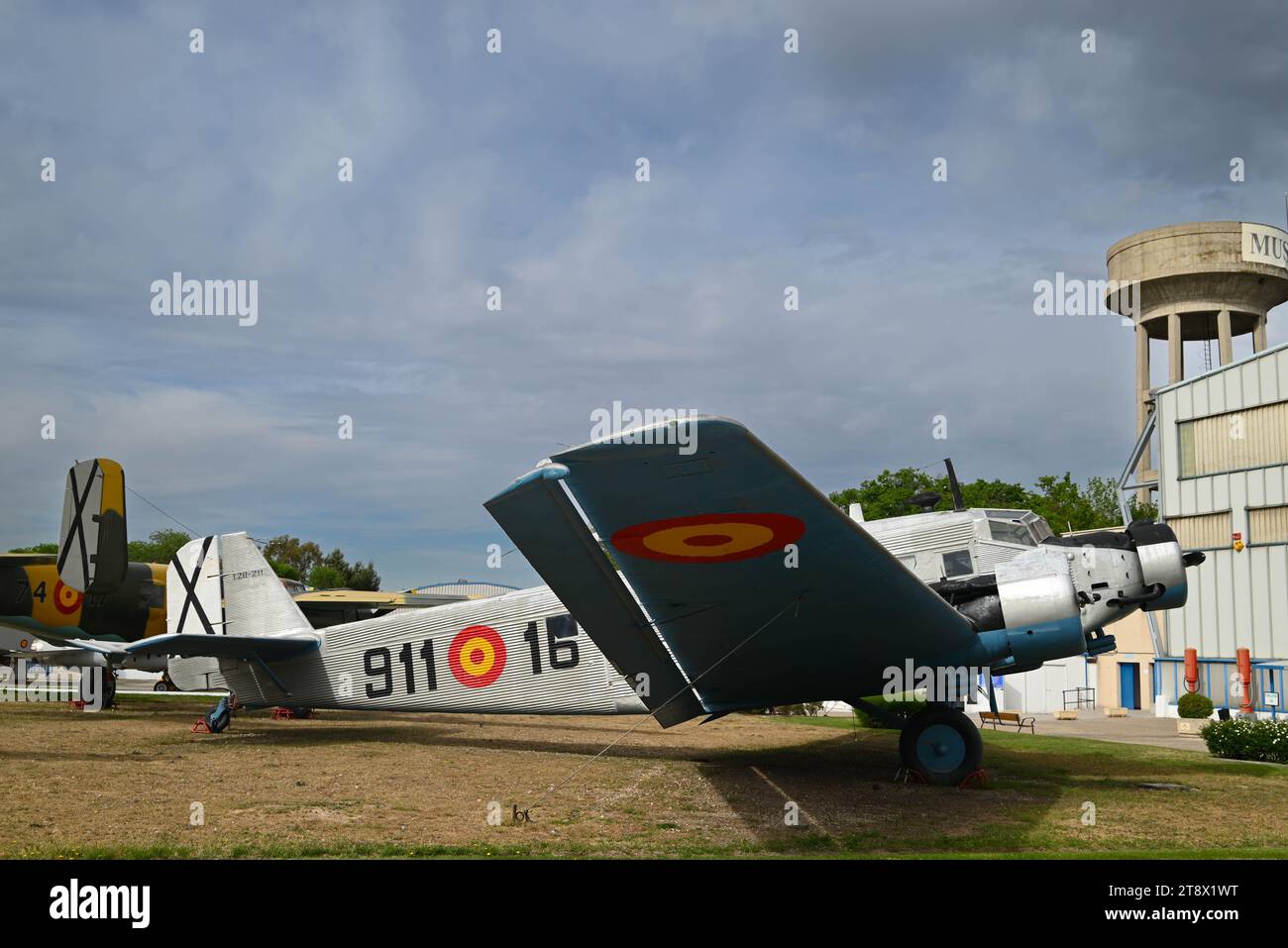 An antiquated aircraft stands in front of a structure alongside other ...