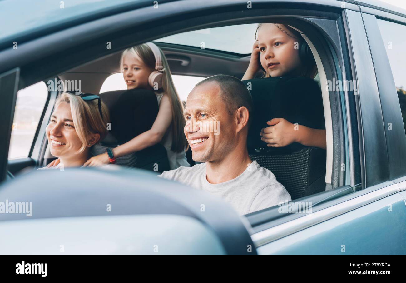 Happy smiling young couple with two daughters inside car during auto trop. They are smiling, and ...