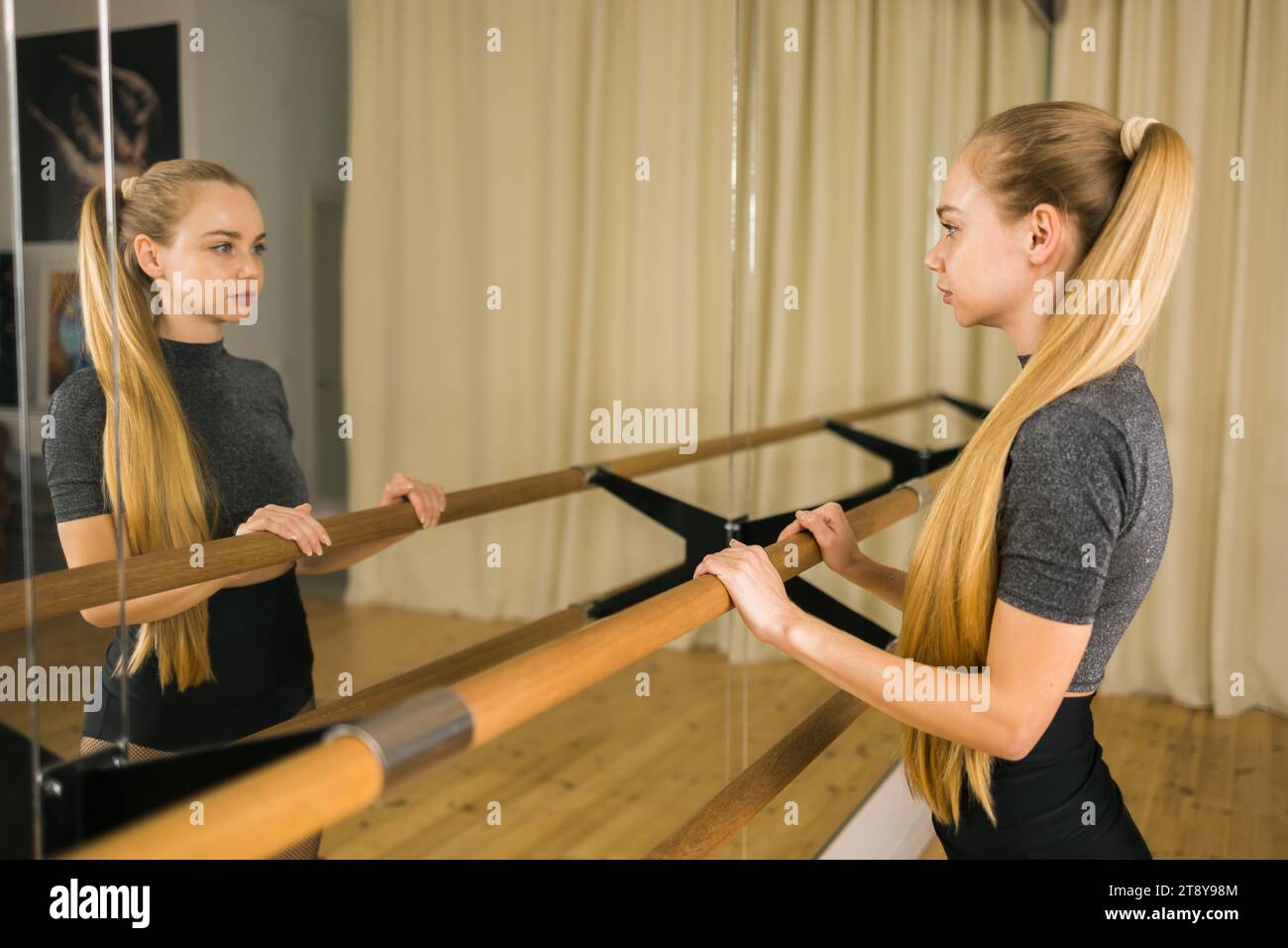 Female ballet dancer resting at barre and mirror in dance studio ...