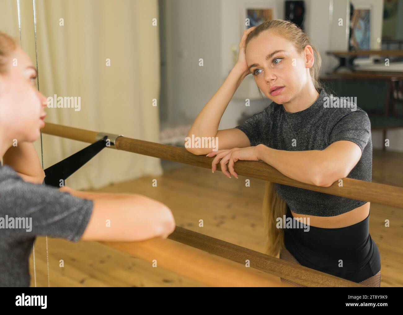 Female ballet dancer resting at barre and mirror in dance studio ...