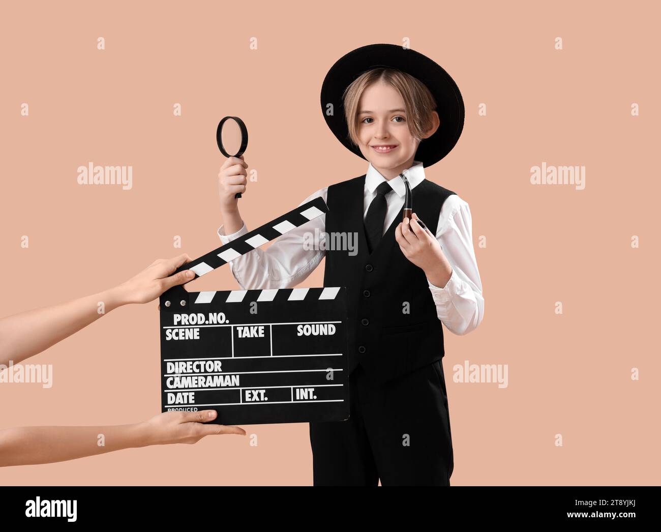 Little actor playing detective and hands with movie clapper on beige ...