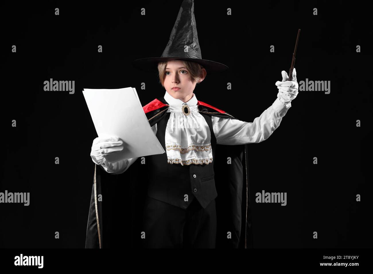 Little actor dressed as magician with film script on dark background ...