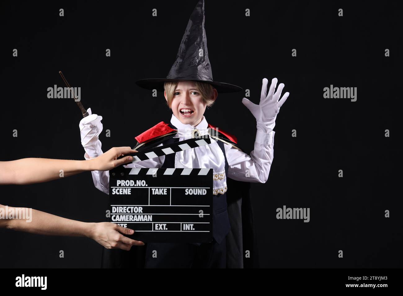 Little actor dressed as magician and hands with movie clapper on dark ...