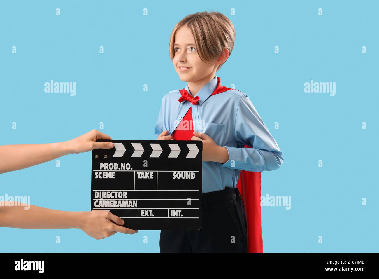 Little actor dressed as superhero and hands with movie clapper on blue ...