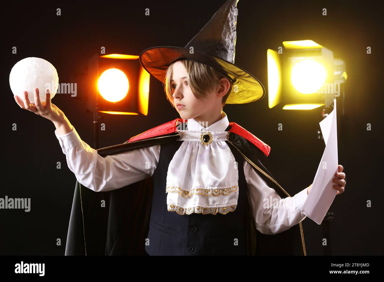 Little actor dressed as magician with film script on dark background ...