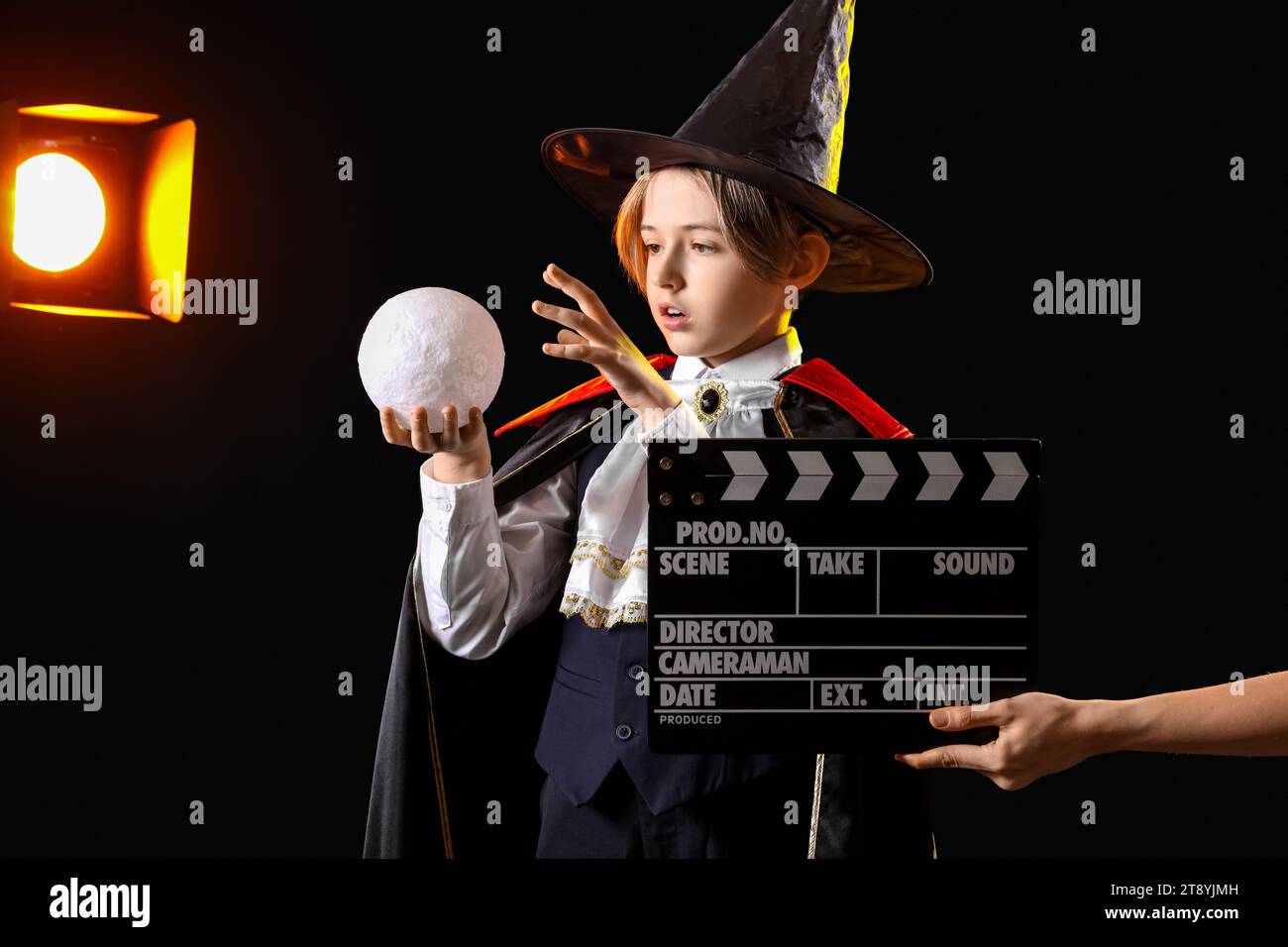 Little actor dressed as magician and hand with movie clapper on dark ...
