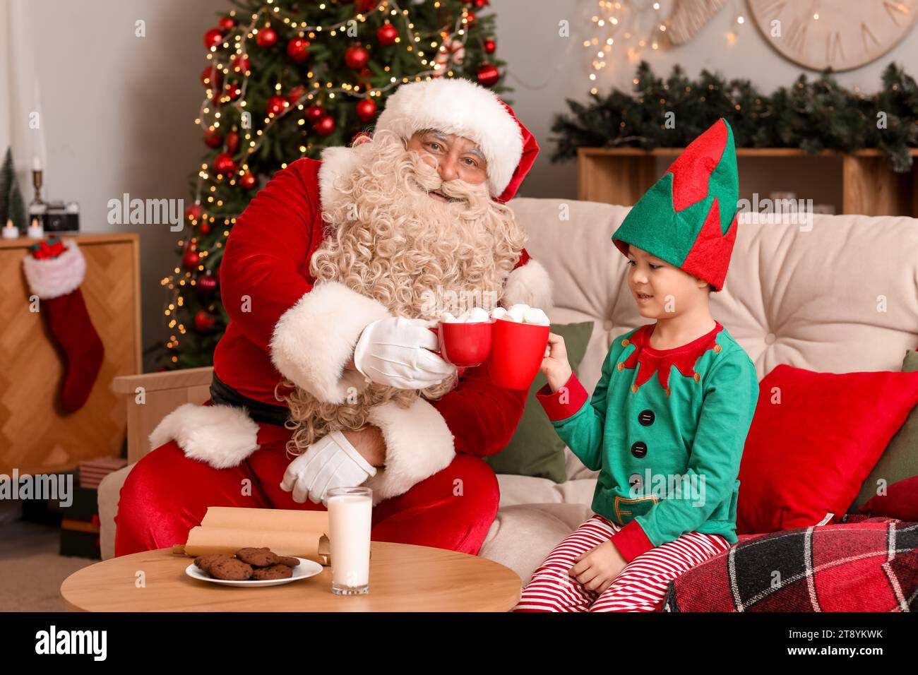 Santa Claus and cute little elf drinking hot chocolate with ...