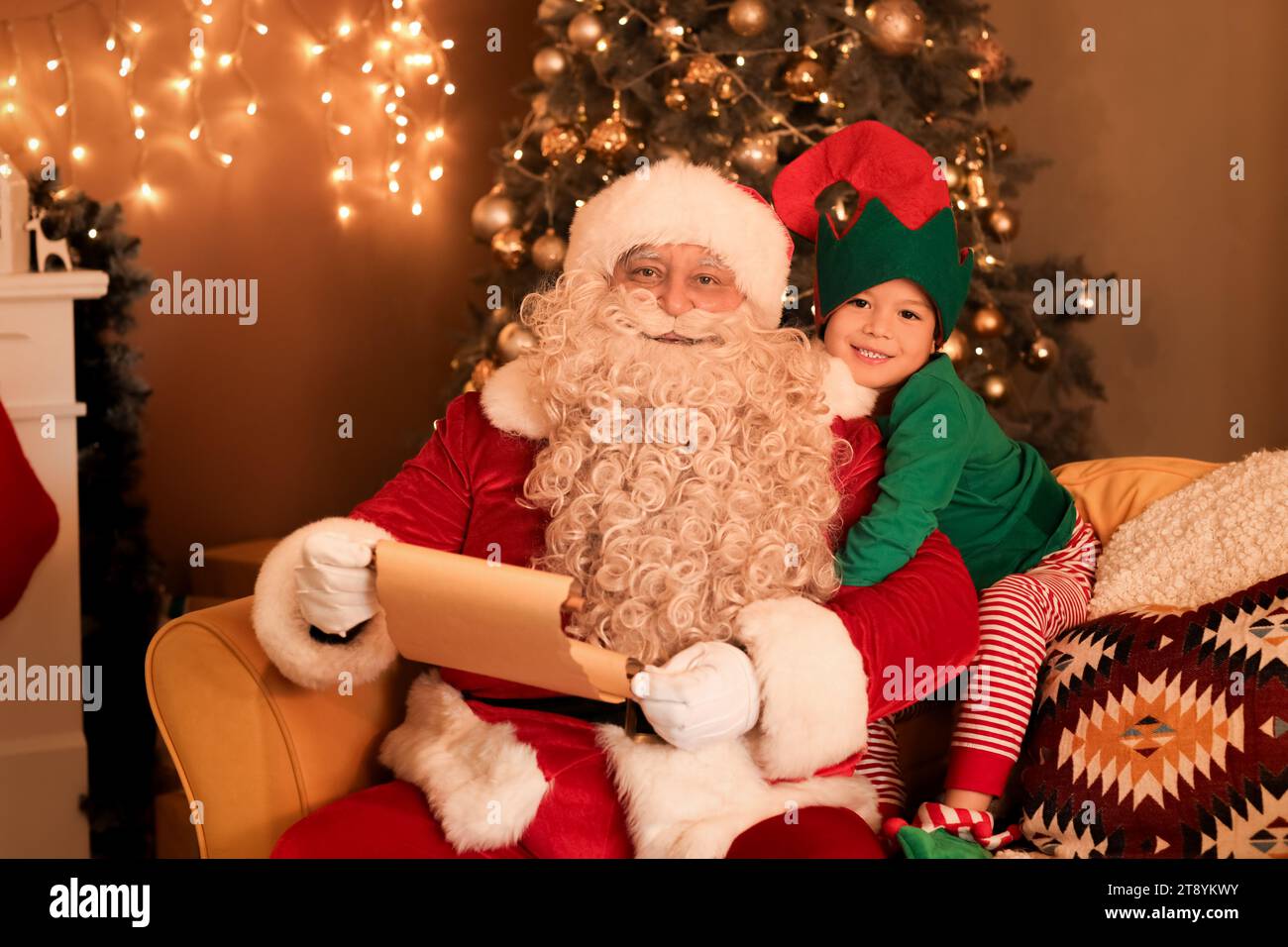 Santa Claus with cute little elf reading letter at home on Christmas ...
