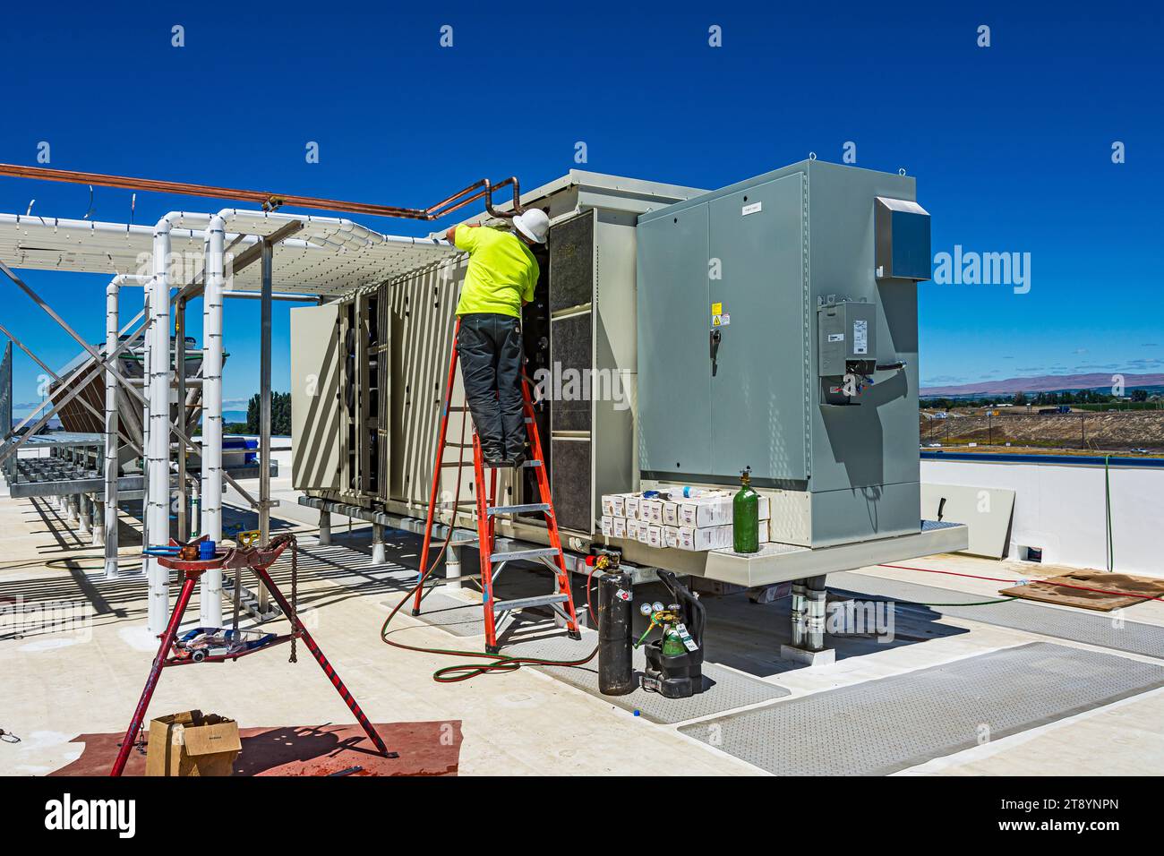 Construction worker brazing copper pipes at a compressor housing on the ...