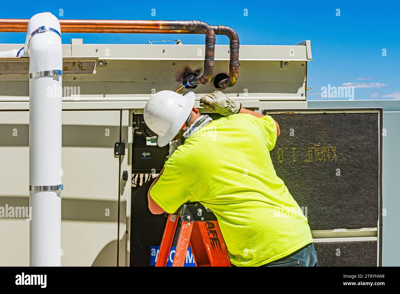 Construction worker brazing copper pipes at a compressor housing on the ...