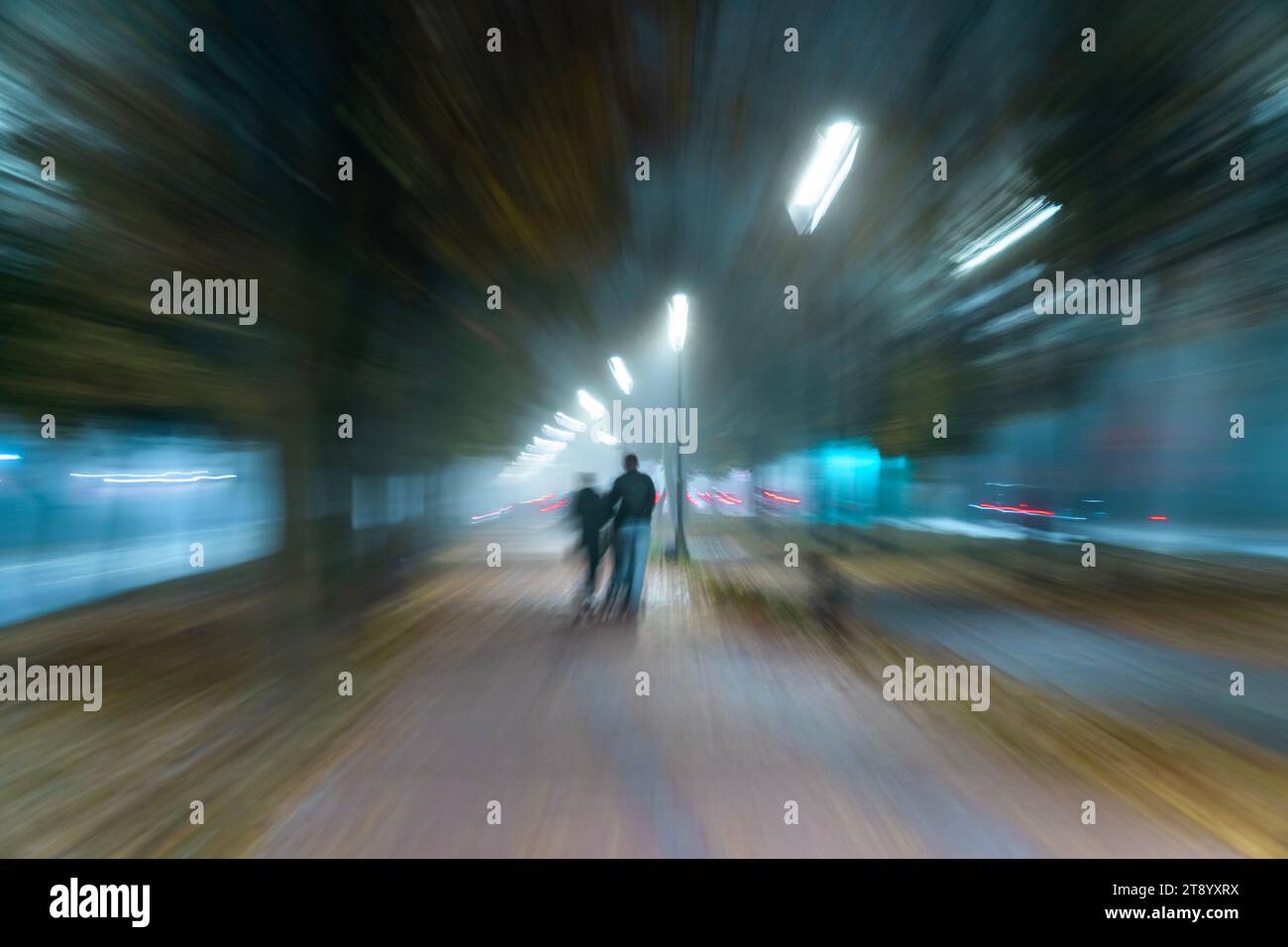 People walk along the city alley in the evening. Light from cars and ...