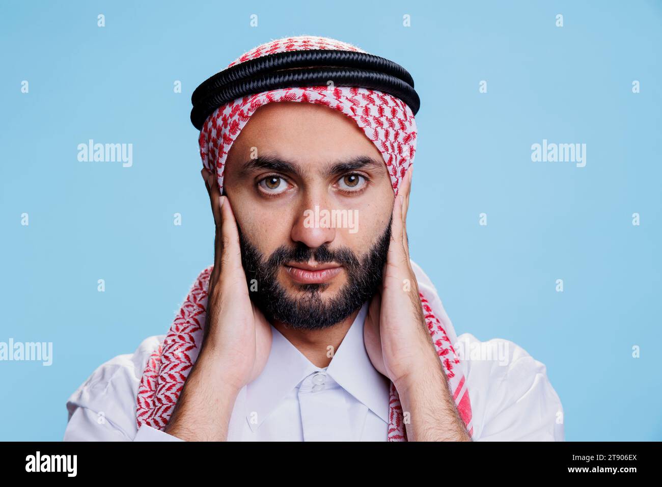 Muslim man closing ears with palms while showing hear no evil three ...