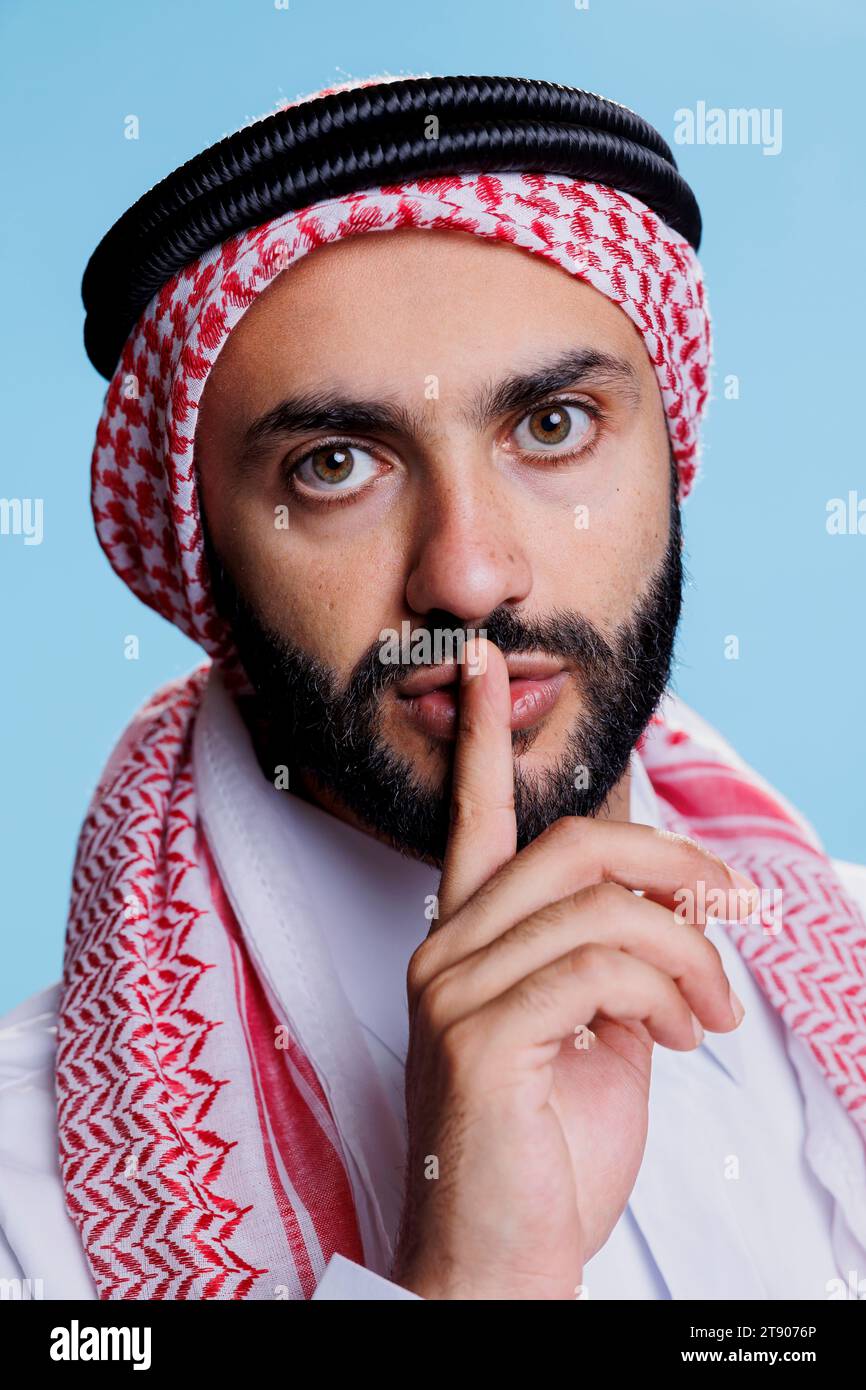 Man wearing muslim headscarf signaling for silence with hushed finger ...