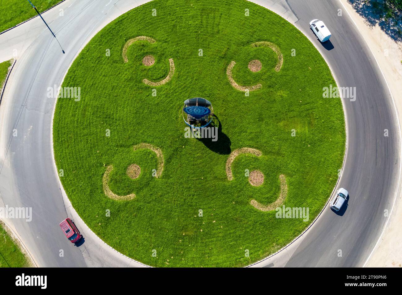 Top view of a road junction with a roundabout around a green flower bed ...