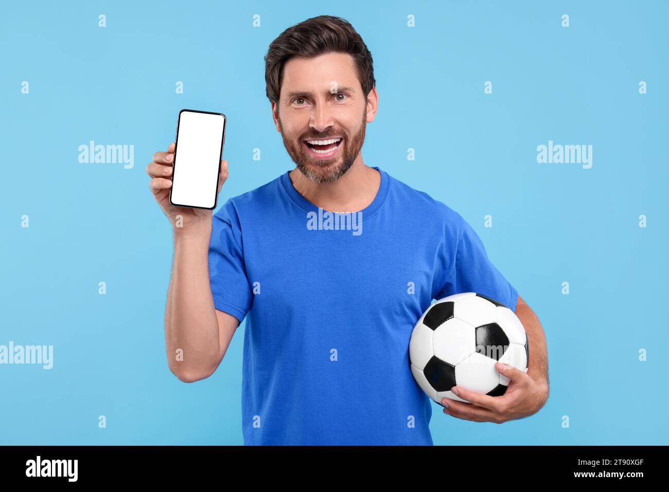 Happy sports fan with soccer ball and smartphone on light blue ...