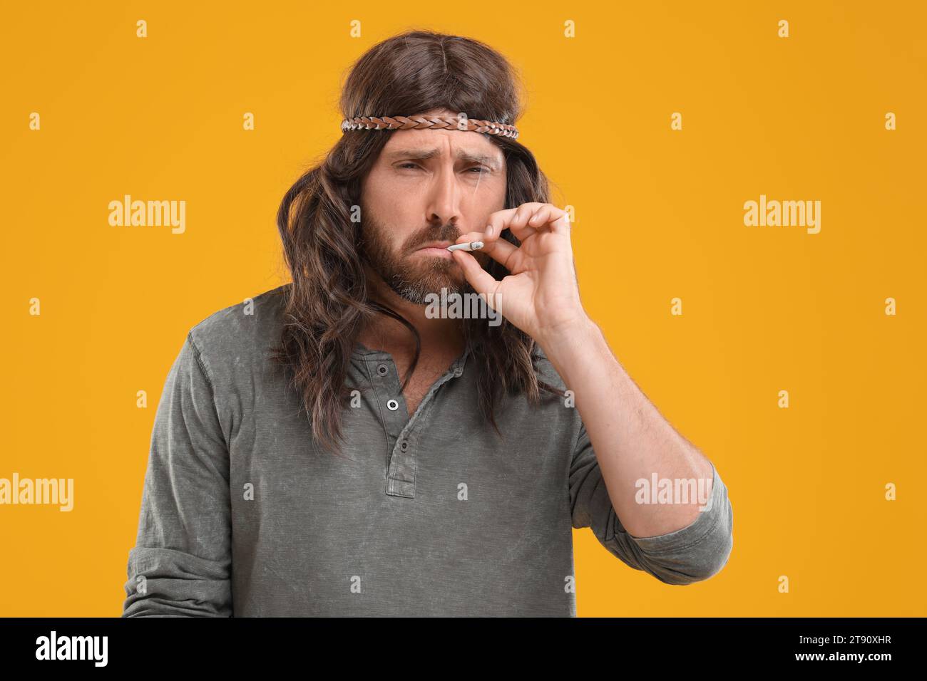 Hippie man smoking cigarette on orange background Stock Photo - Alamy