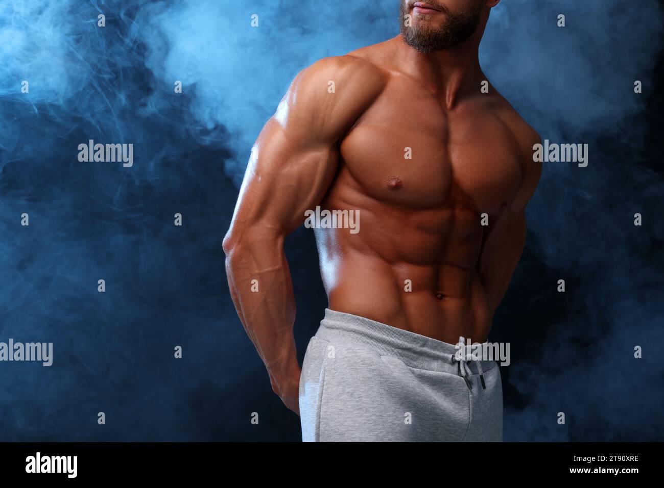 Young bodybuilder with muscular body in smoke on color background ...