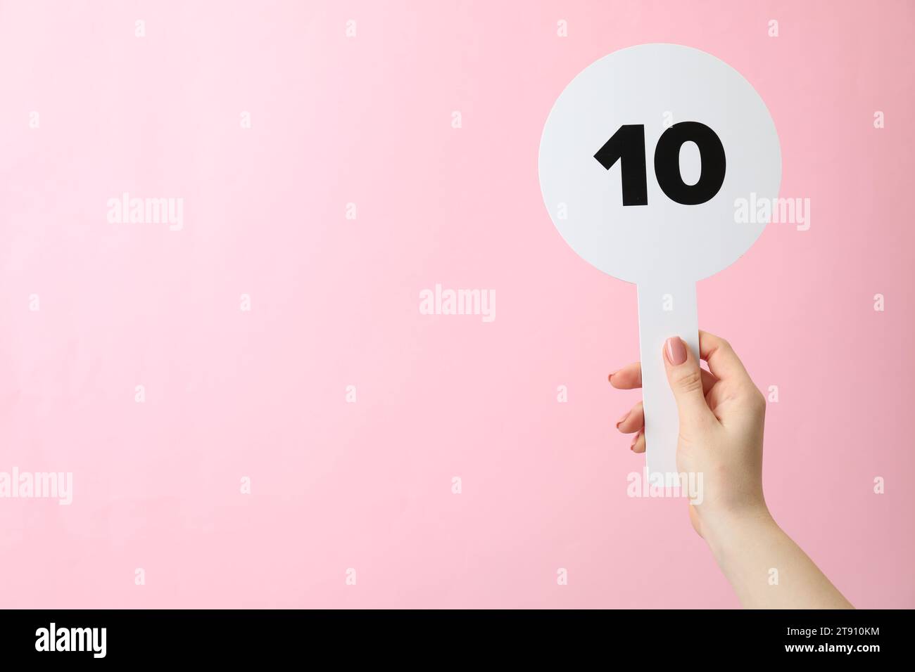 Woman holding auction paddle with number 10 on pink background, closeup ...
