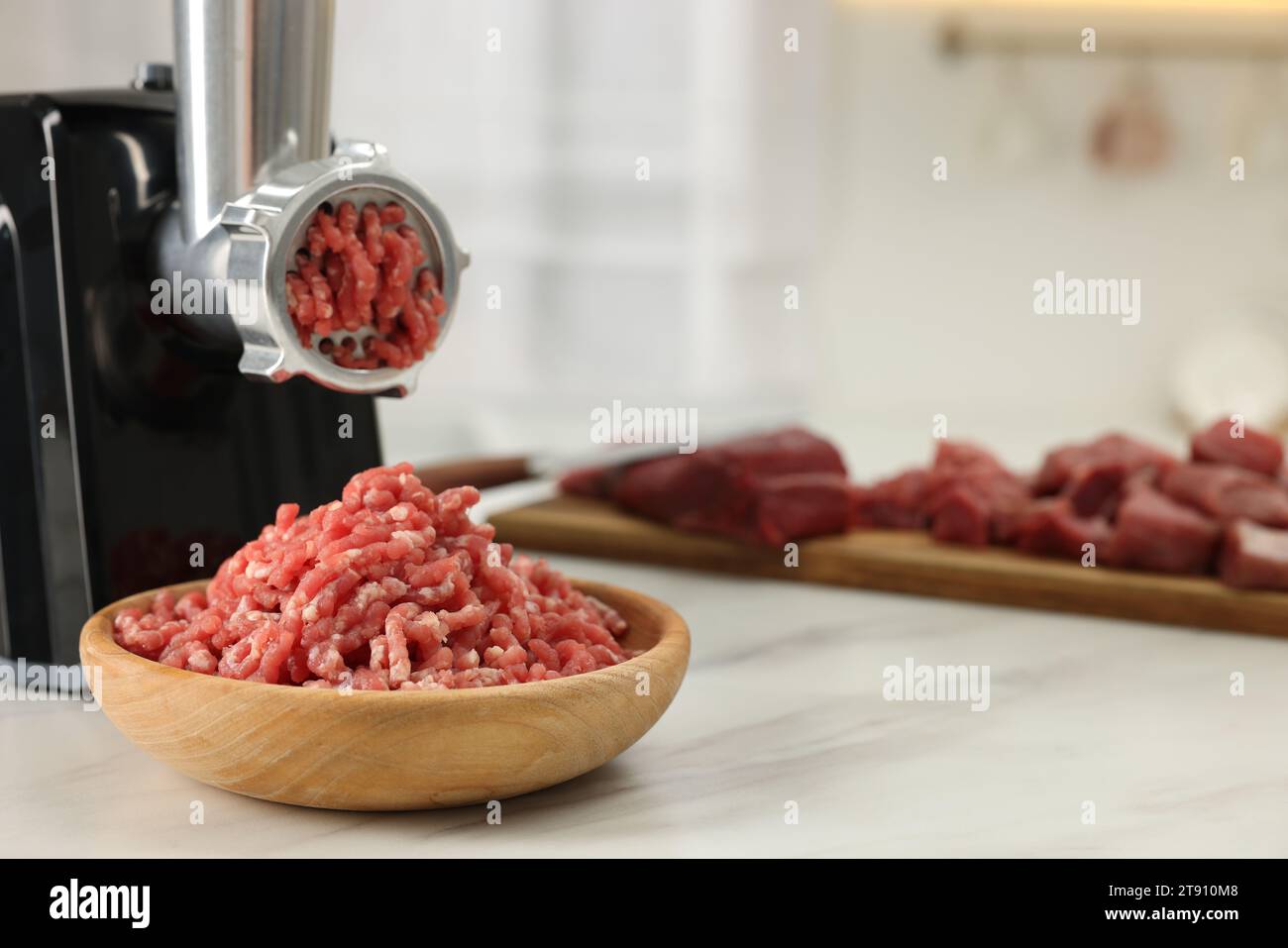 Electric meat grinder with minced beef on white marble table in kitchen ...