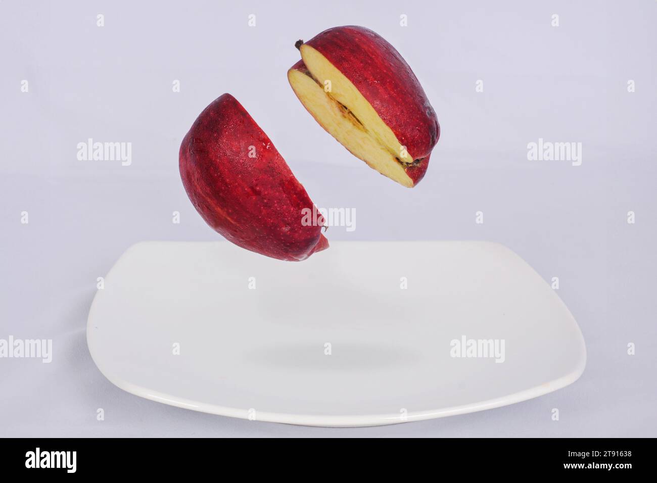 an apple split in the air on a white plate Stock Photo - Alamy