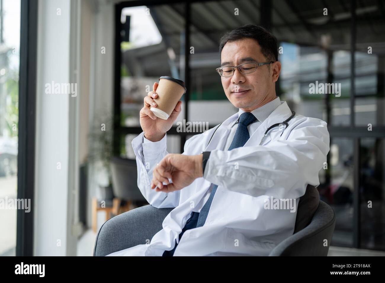 A professional senior male doctor is checking time on his wristwatch ...