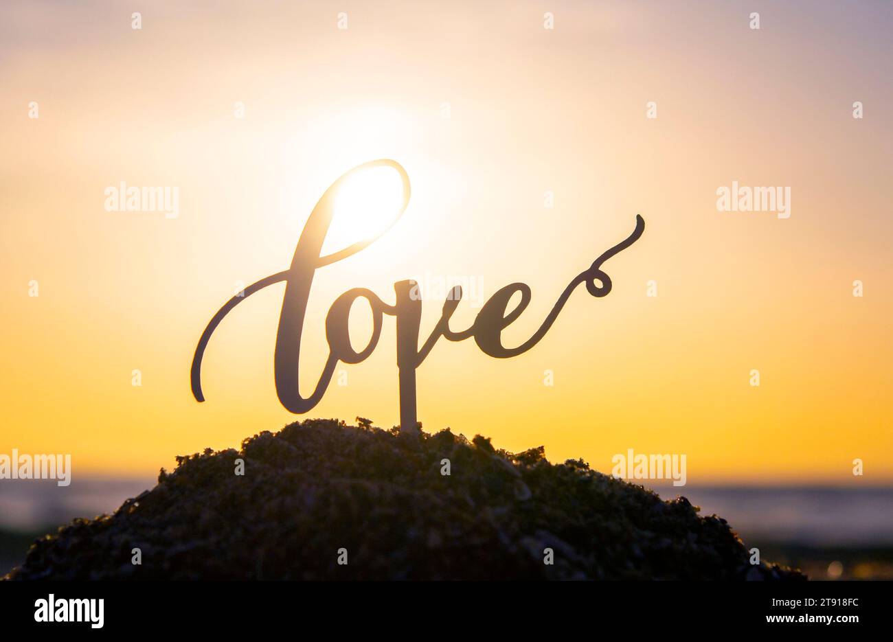 Black outlines of word Love at dawn and sunset on sky on seashore ...