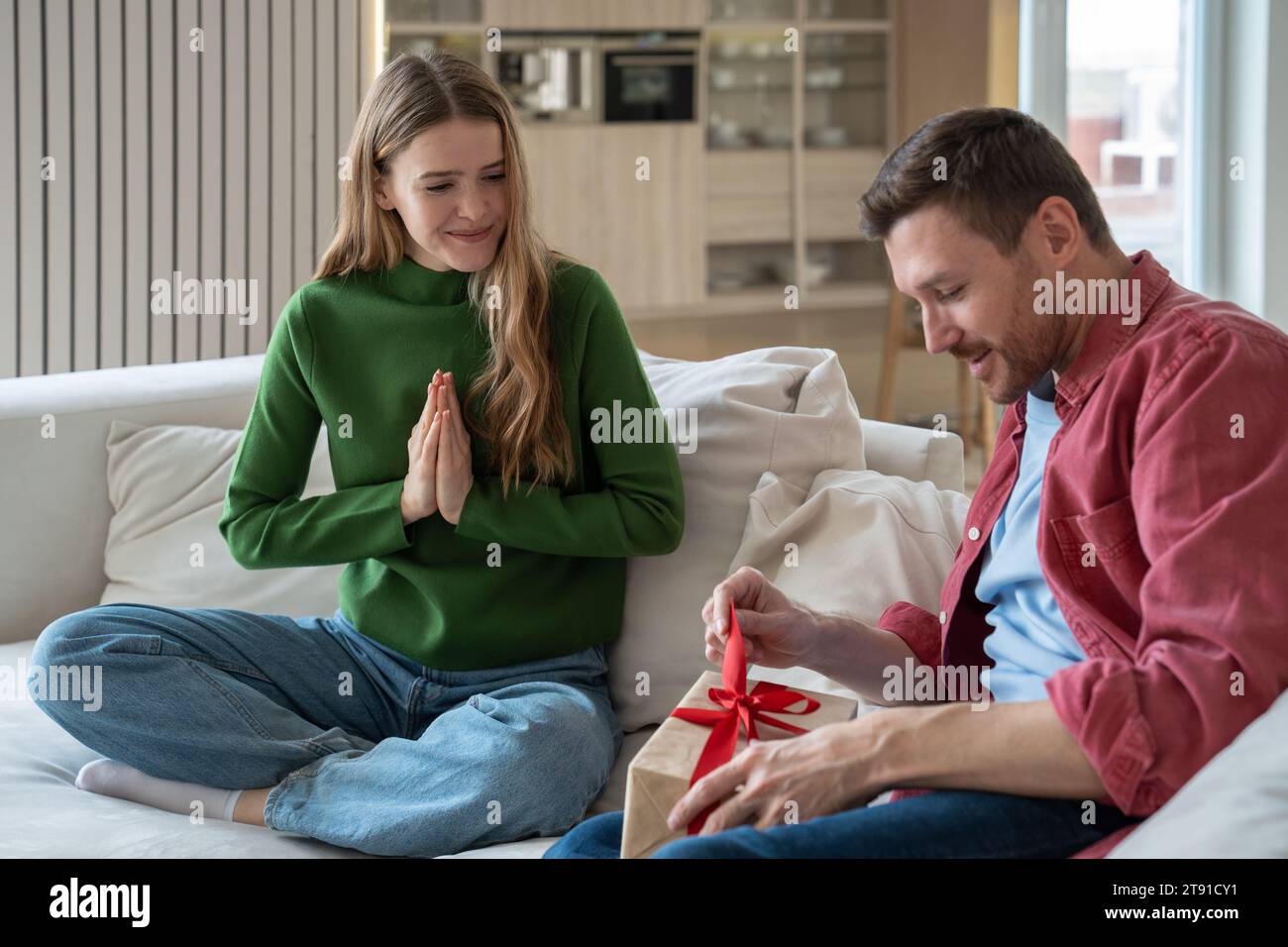 Surprised man unpack gift present, woman wait sitting on couch near ...
