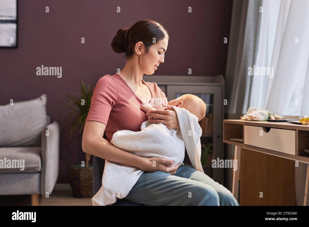 Side view portrait of happy young mother rocking baby to sleep at home ...