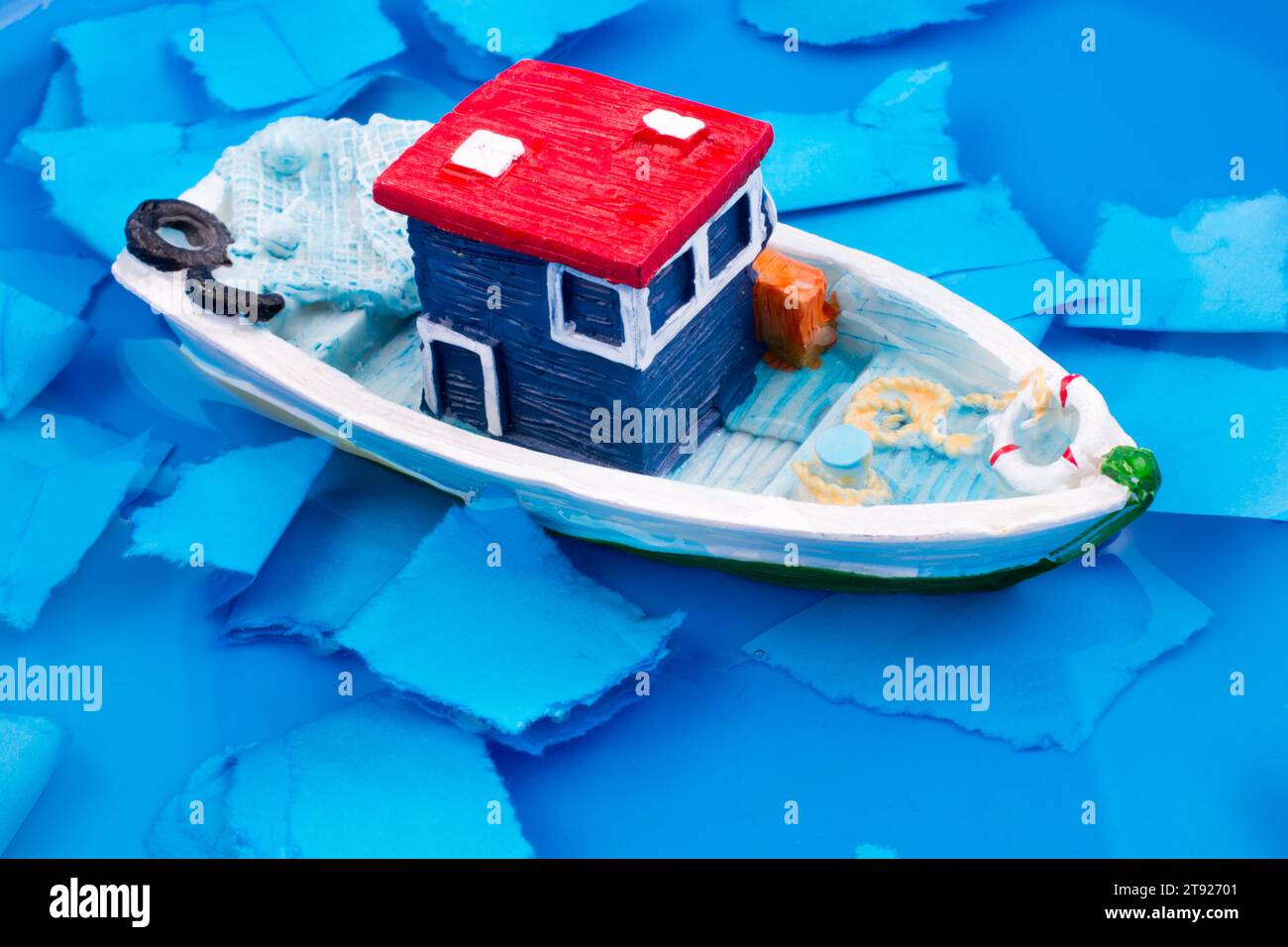 Little model fishing boat in water with torn paper on a blue background ...