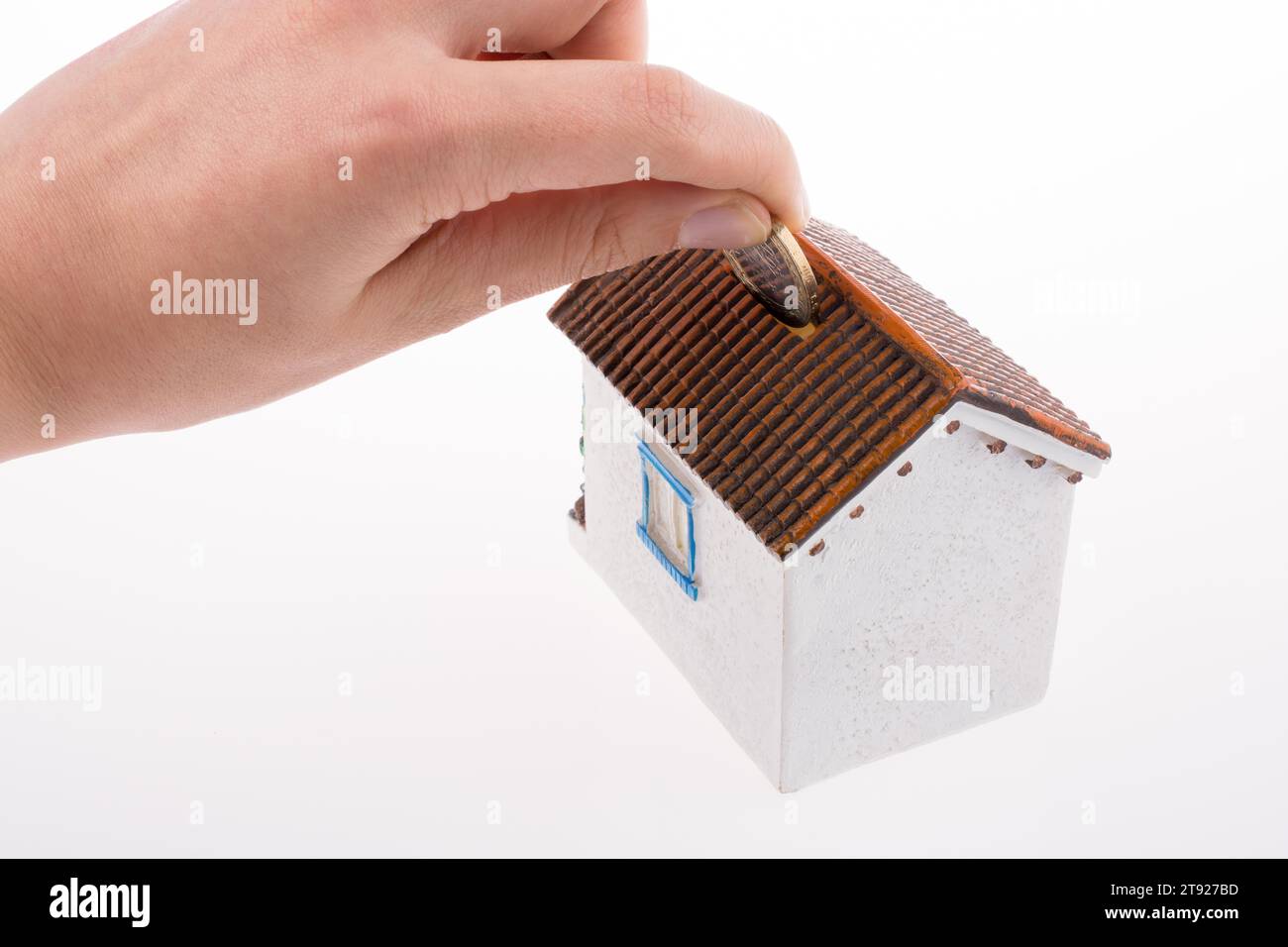 Hand dropping coin into the moneybox in the shape of a model house ...