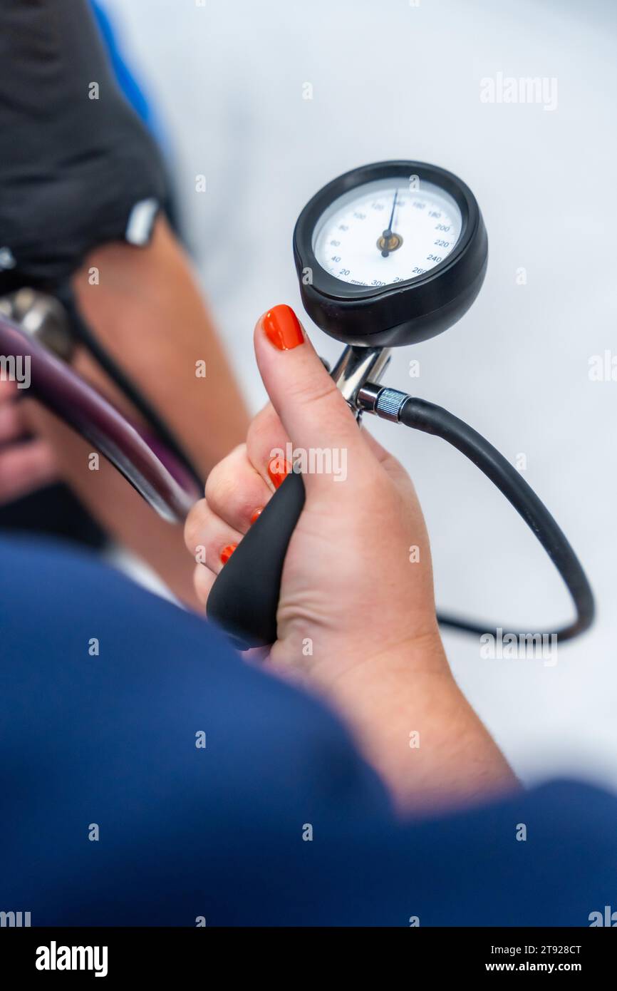 Doctor measuring the blood pressure of a woman sitting on a stretcher ...