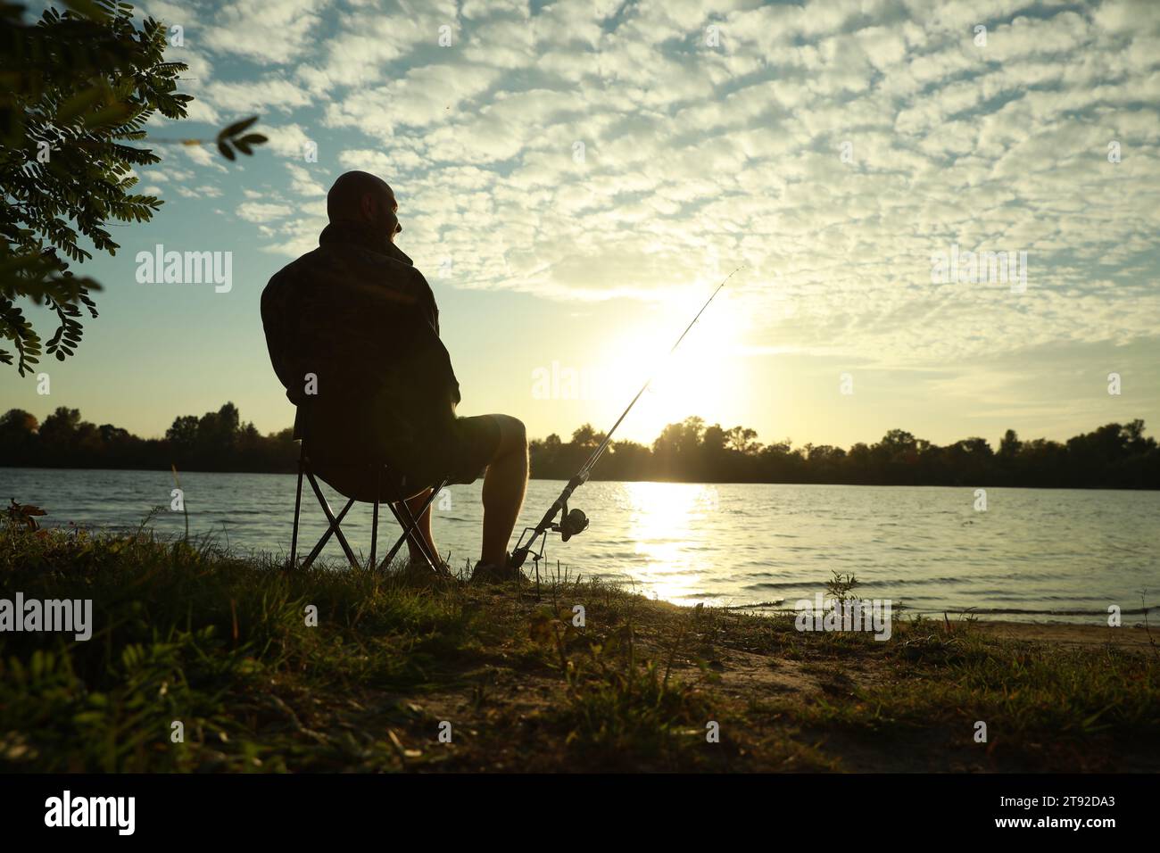 Fisherman with rod sitting on folding chair and fishing at riverside ...