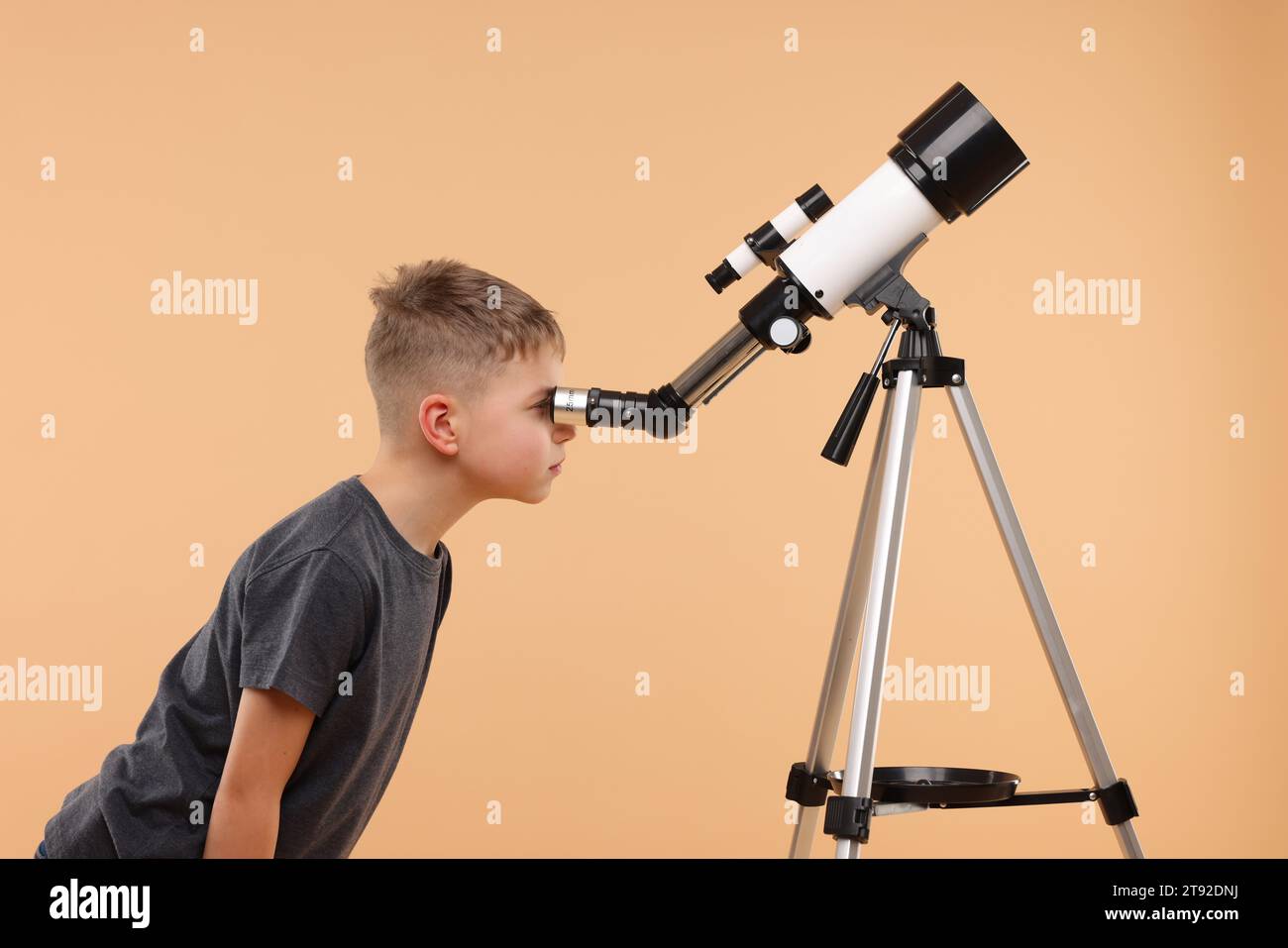 Little boy looking at stars through telescope on beige background Stock ...