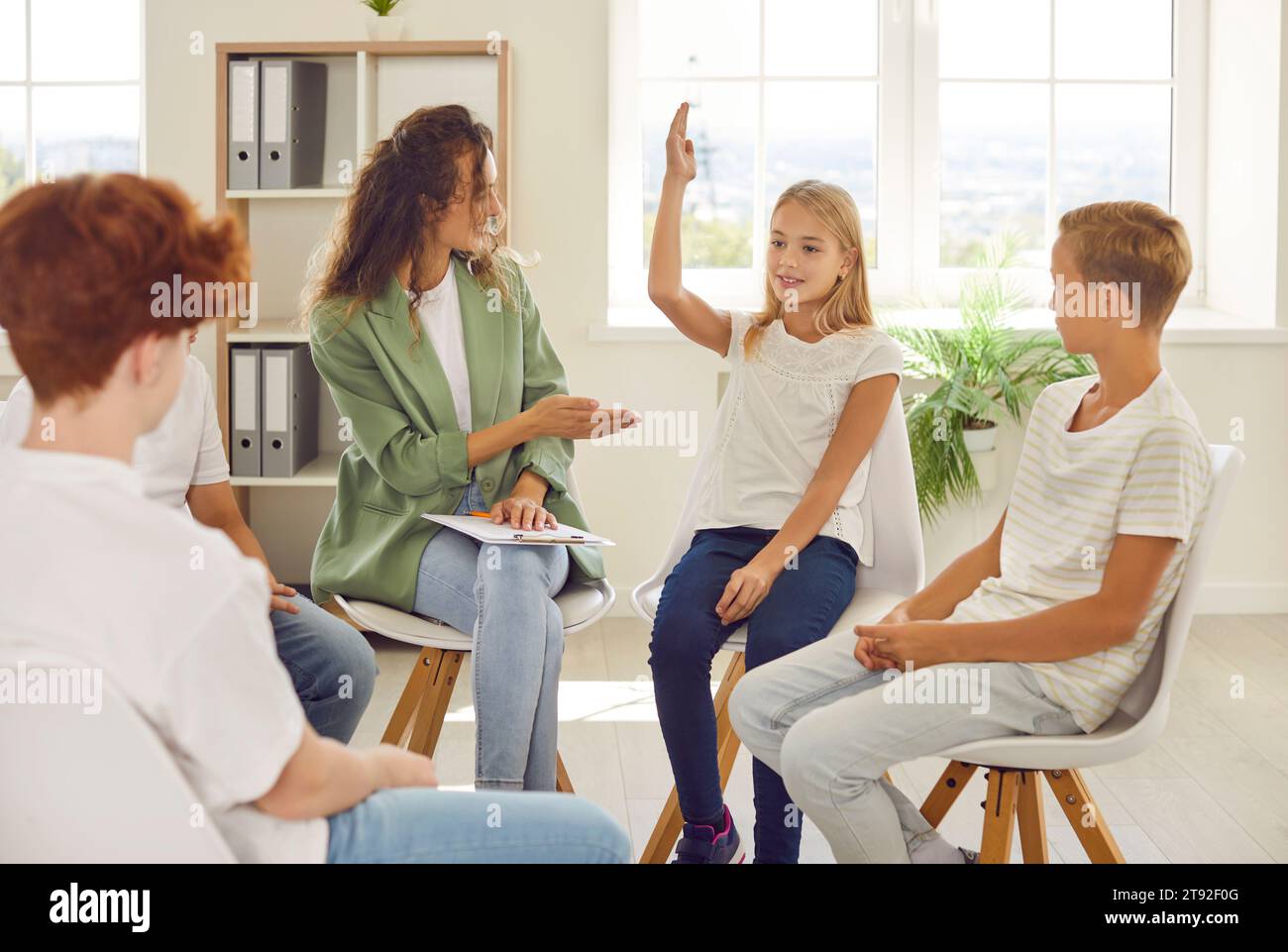 School girl raising hand up to answer a question during group therapy ...