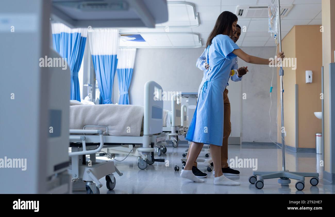 Diverse female patient walking with drip and male doctor helping in ...