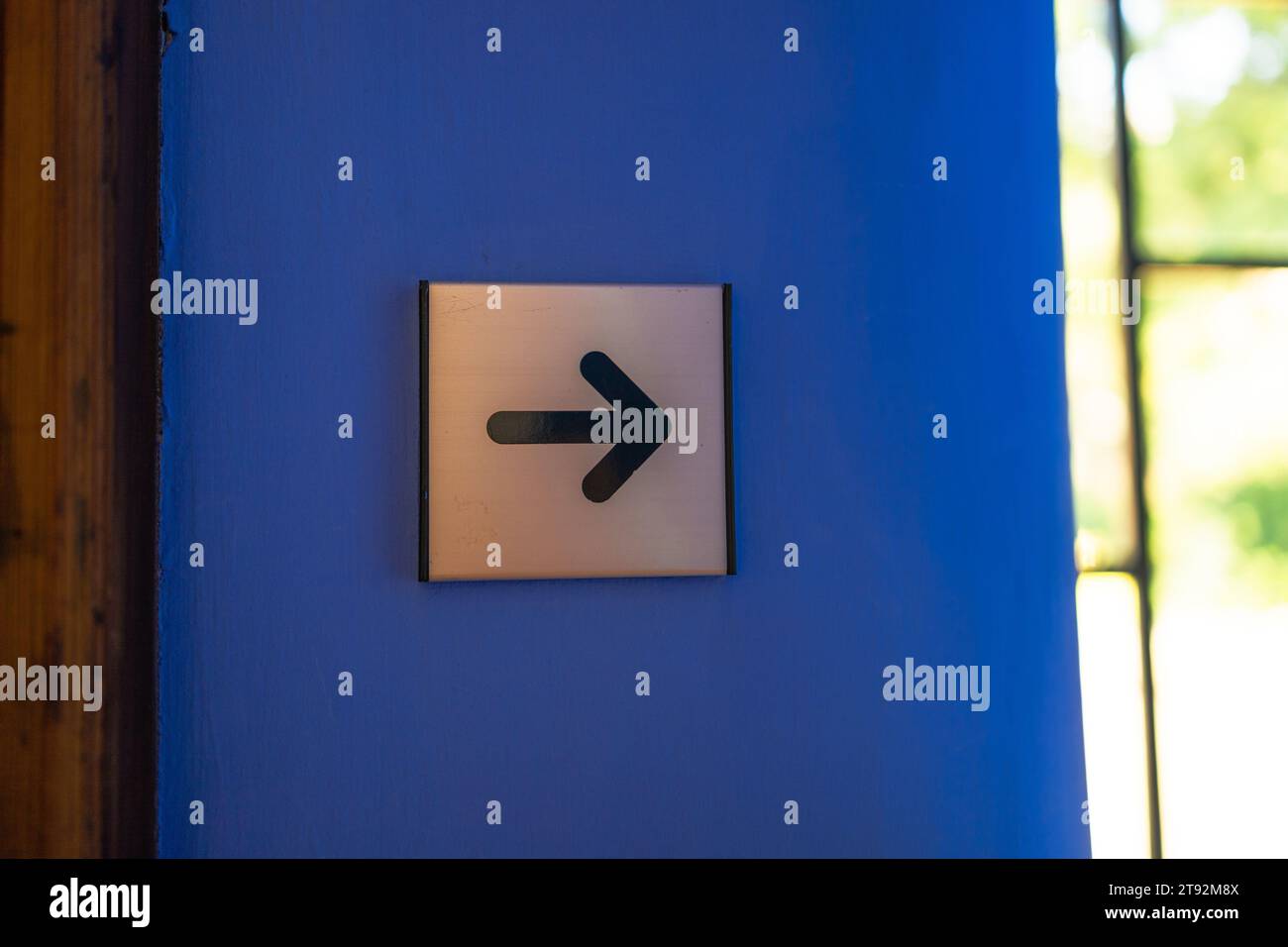 Black arrow sign hanging against blue wall for direction, pointing left ...