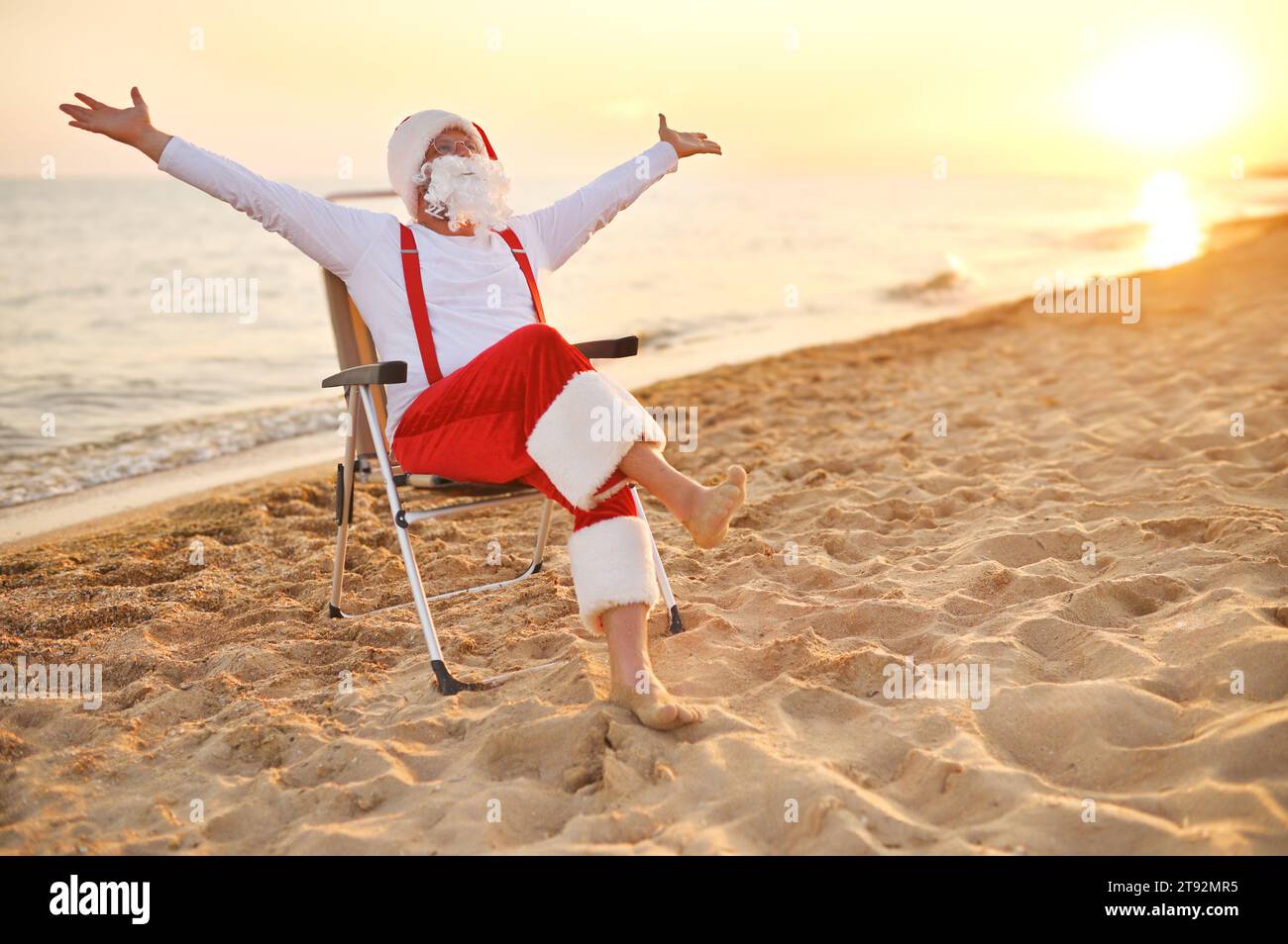 Santa barefoot in red suspenders sitting on a chaise lounge resting ...