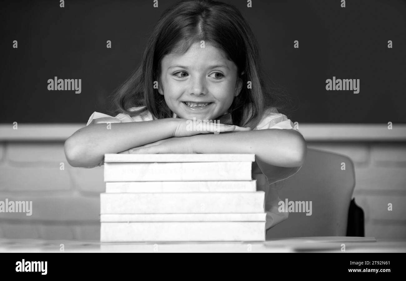 Smiling girl sitting at the desk and holding hands on the books in the ...