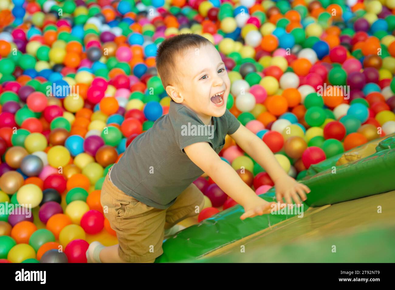 Happy smiling toddler boy climbs up on a slide in a children's room or ...