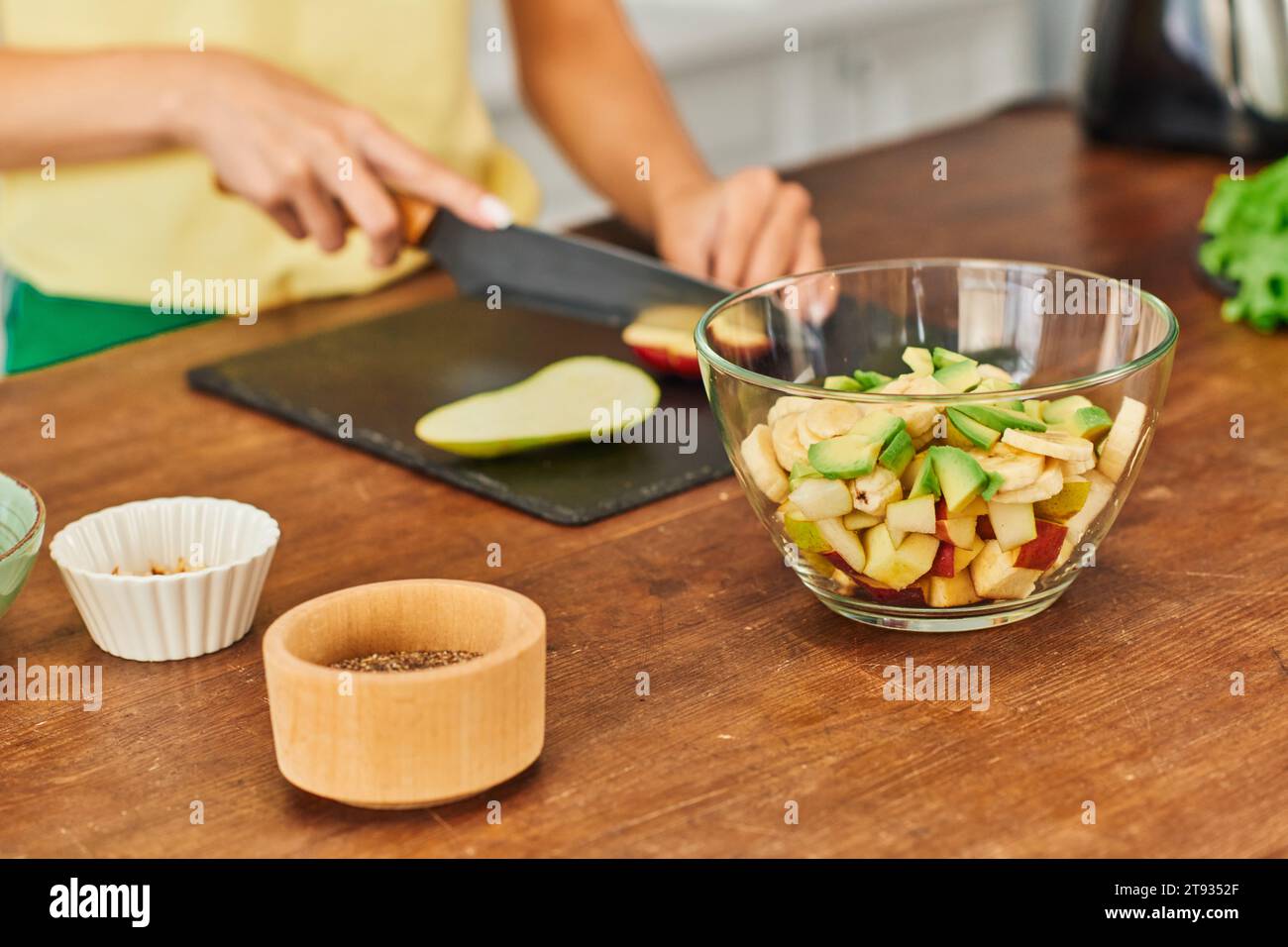 bowl with chopped fruits near cropped woman cutting pear on blurred ...