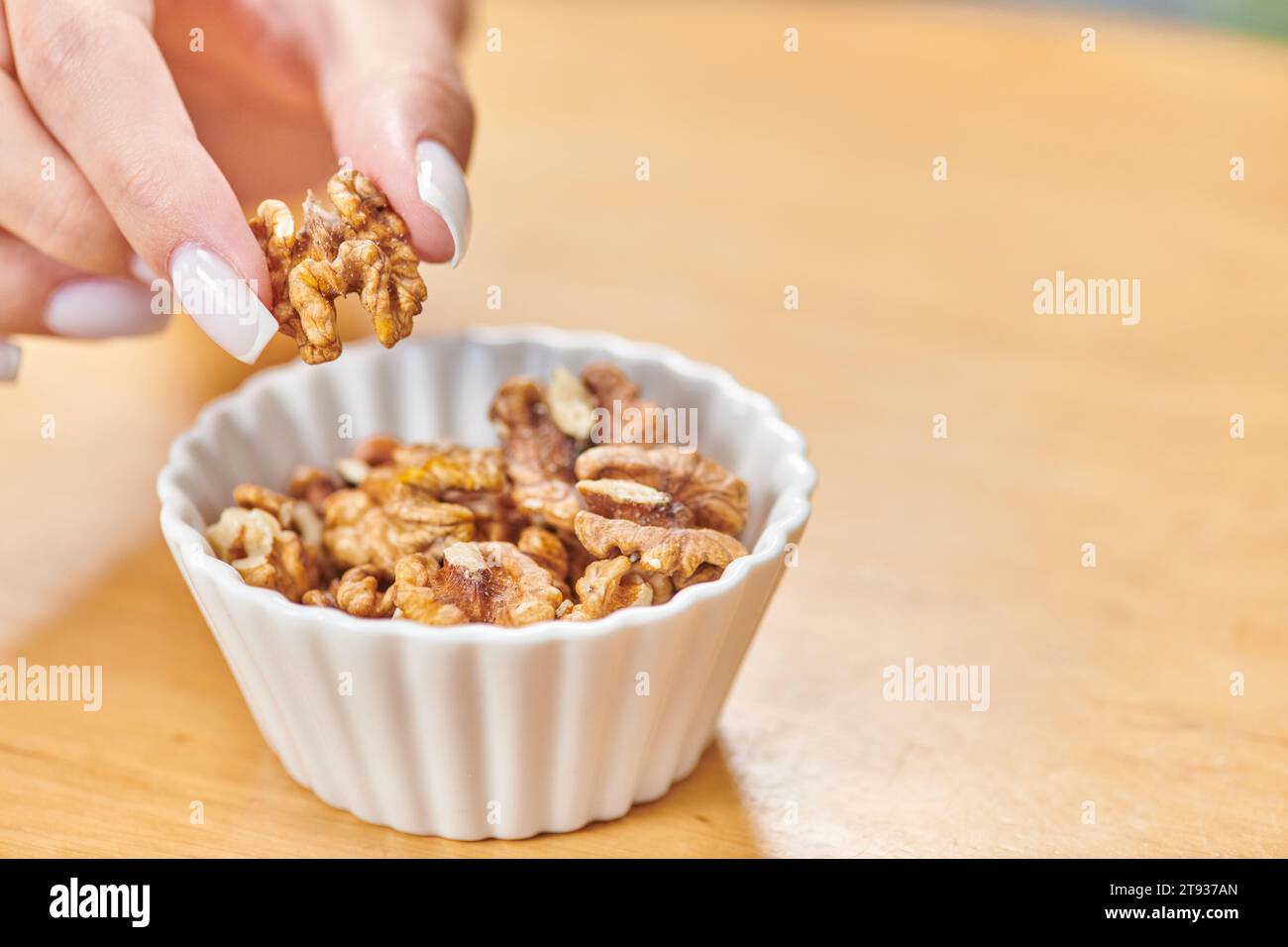 cropped view of female hand taking walnut from white ceramic bowl, high ...