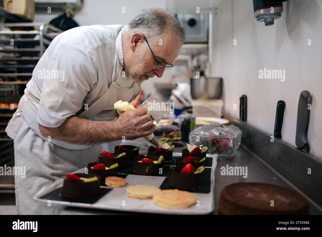 Senior pastry chef with white apron and white hair decorating cakes ...