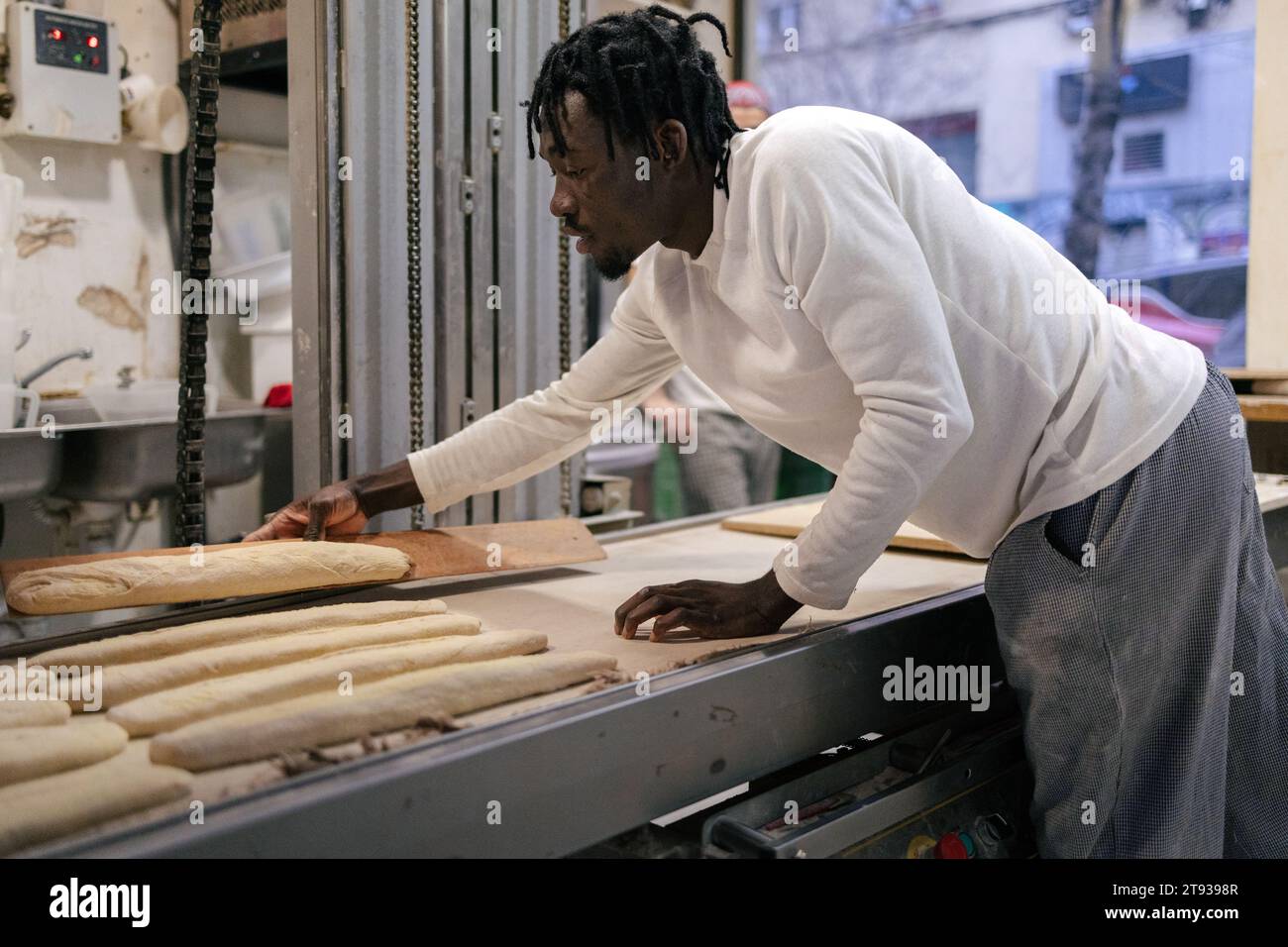 Black baker dressed in white clothes placing a loaf of bread with a ...
