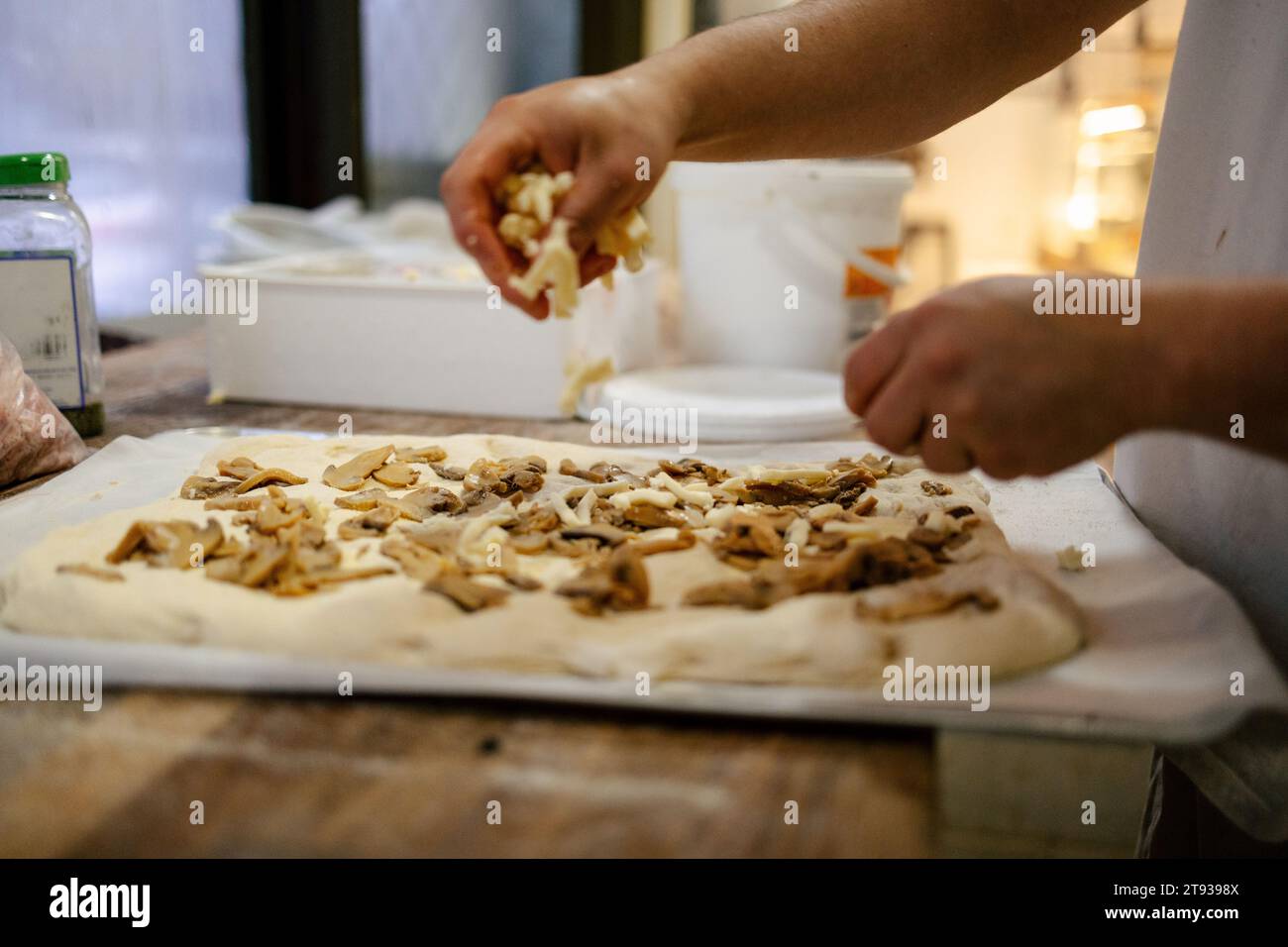 Close-up of a person's hands adding toppings to a pizza in a bakery ...