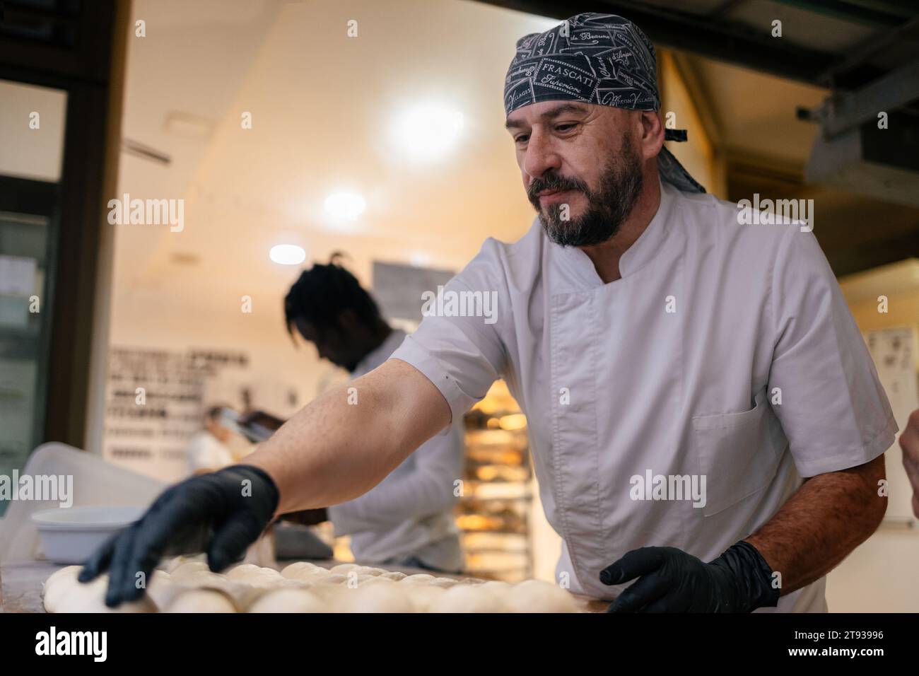 Adult baker dressed in white clothes and a black cap making balls of ...