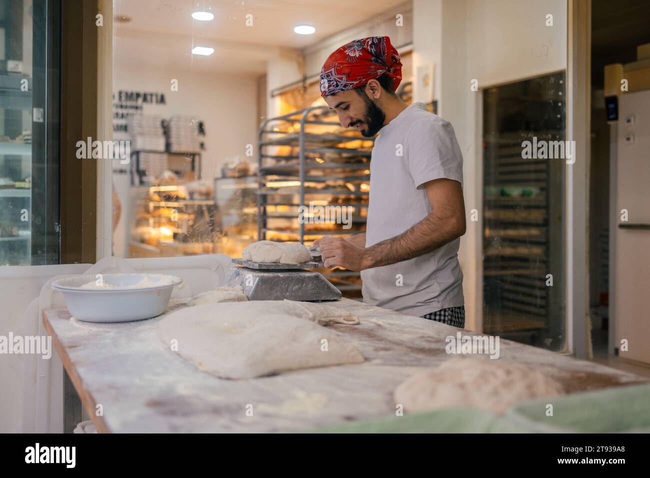 Young arabic baker dressed with white clothes and a red hat cutting ...